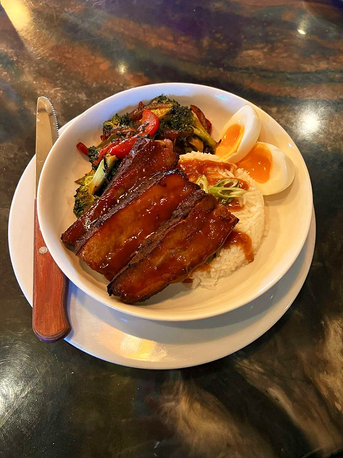 This isn't just pork belly – it's a glistening masterpiece of meat candy atop rice with vegetables and a perfectly halved egg standing guard.