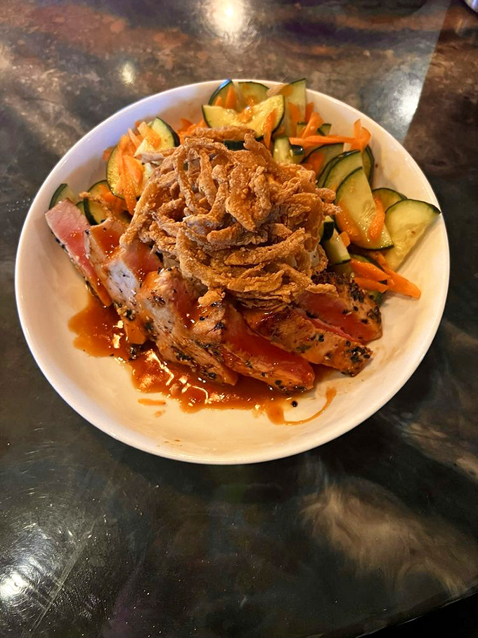 Sliced tuna resting on a bed of vibrant vegetables with crispy onions on top – like a protein superhero wearing a cape of freshness.