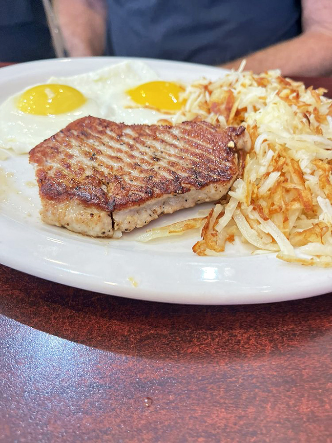 The breakfast trifecta! This plate's got more star power than a Hollywood red carpet: a show-stopping pork chop, eggs with yolks of gold, and hash browns crispier than a new dollar bill.