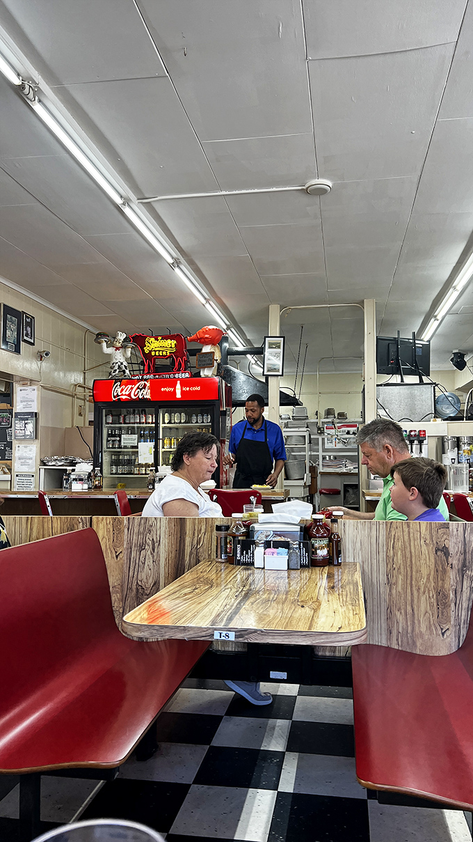 Red vinyl booths and wooden tables—the stage where barbecue memories are made. That bottle of sauce stands ready, like a conductor waiting for the symphony to begin.