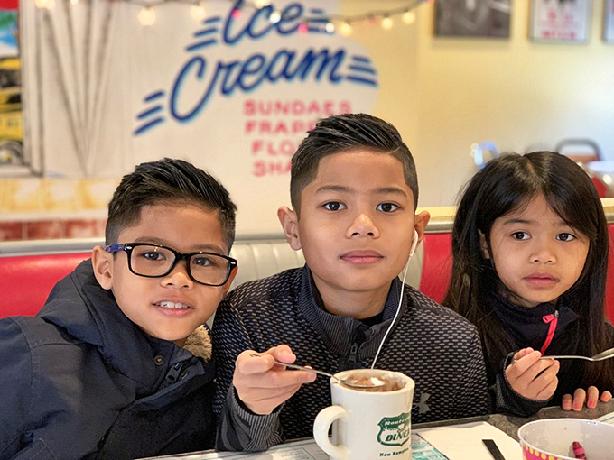 The image shows diners enjoying their meals in a retro-styled setting. The decor and atmosphere contribute to a classic American diner experience.