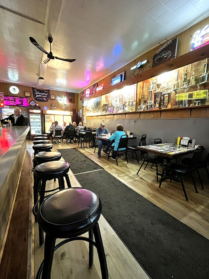 Inside, wood paneling and neon beer signs create the perfect time capsule where conversations flow as freely as the cold drinks.