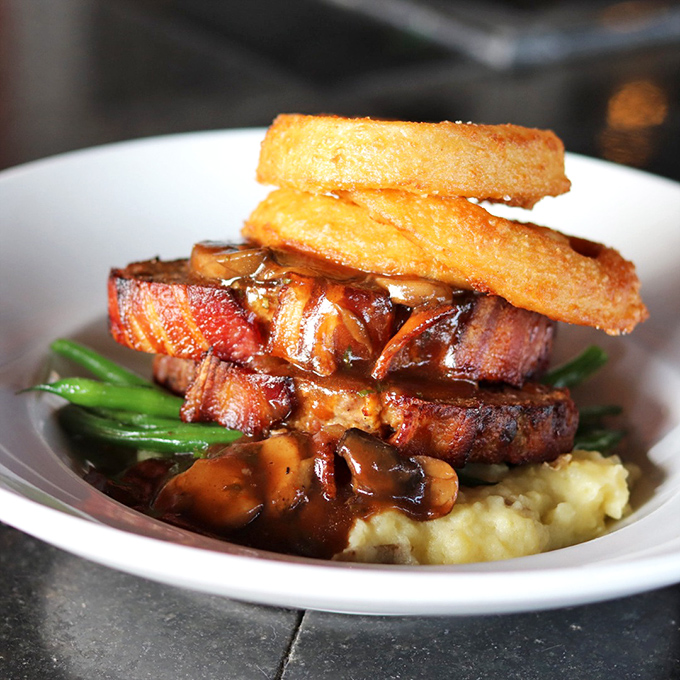 Heaven stacked vertically: pork tenderloin, crowned with crispy onion rings, bathed in savory gravy. Architecture that would make Frank Lloyd Wright put down his pencil and pick up a fork.