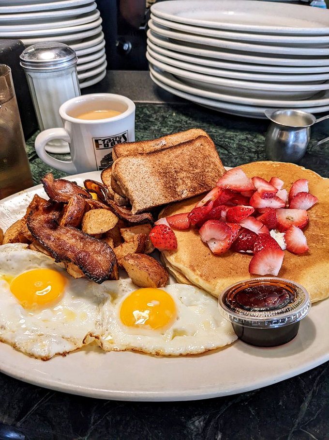 Breakfast nirvana achieved: sunny-side up eggs, crispy bacon, home fries, toast, and pancakes topped with fresh strawberries.