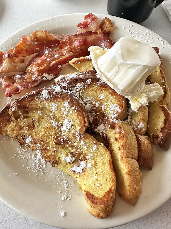 French toast that's achieved golden-brown perfection, dusted with powdered sugar and crowned with a dollop of butter that's slowly surrendering to the warmth.