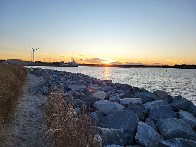 Sunset paints the breakwater in golden hues as ships pass in the distance. This rocky shoreline offers front-row seats to nature's nightly masterpiece.
