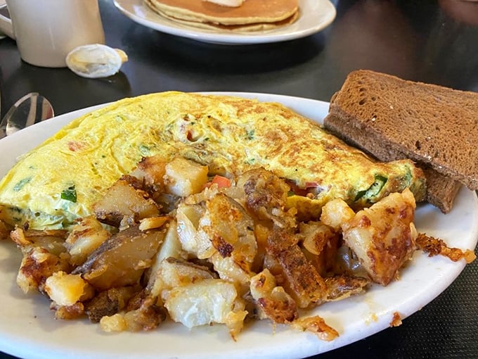Behold, the omelet that ate Manhattan! This golden masterpiece, bursting with fillings, is flanked by home fries that could start their own fan club.