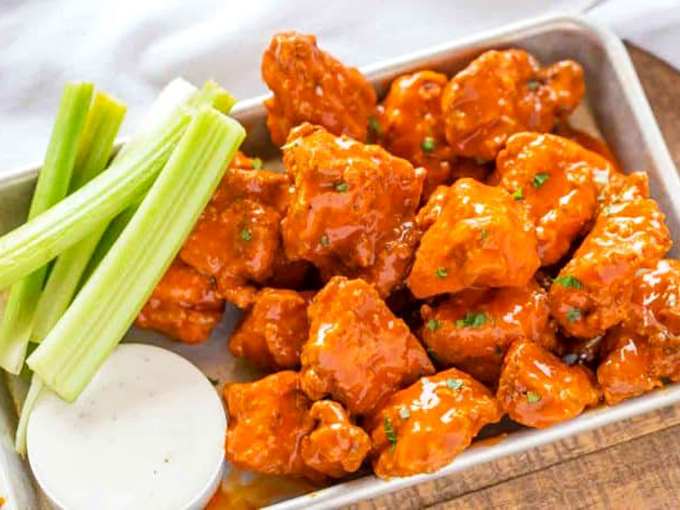 Boneless wings lounging in their sauce bath with celery standing guard. The perfect food for when you want flavor without the commitment of bones.