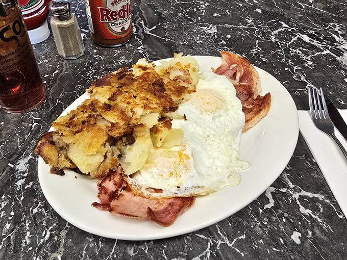 The holy trinity of breakfast: golden hash browns, farm-fresh eggs with runny yolks, and ham sliced thick enough to make your cardiologist wince but your taste buds sing.