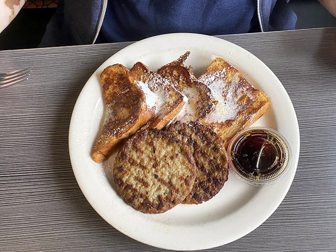 Golden challah French toast dusted with powdered sugar alongside a perfectly griddled sausage patty&mdash;breakfast harmony on a plate.