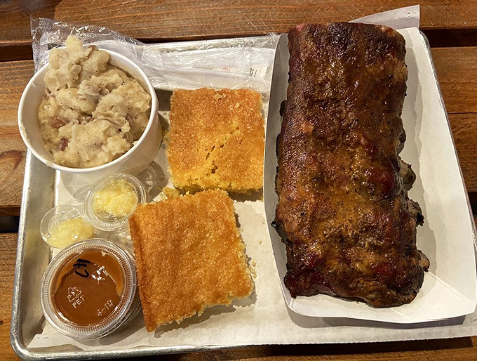 Rib-diculous deliciousness! This half rack is ready for its close-up, flanked by creamy potato salad and cornbread that's begging to soak up every drop of sauce.