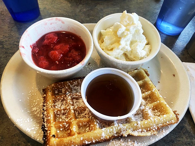 The holy trinity of breakfast: golden waffle, ruby strawberries, and a cloud of whipped cream. It's like a sunrise on a plate!