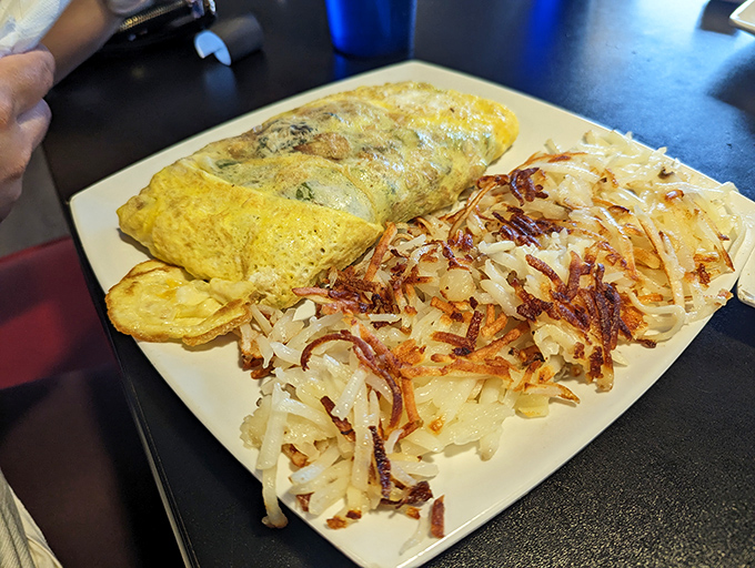 The omelet that launched a thousand road trips, paired with hash browns crisped to mathematical perfection. This plate alone justifies the invention of breakfast.