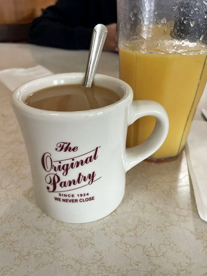 The coffee mug proudly declares "We Never Close"&mdash;a promise as comforting as the amber orange juice standing guard beside it.