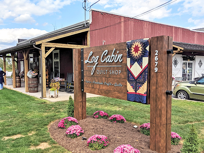 The iconic red barn exterior of Log Cabin Quilt Shop welcomes fabric enthusiasts with its charming quilt block emblem&mdash;a colorful beacon for crafters in Amish Country.