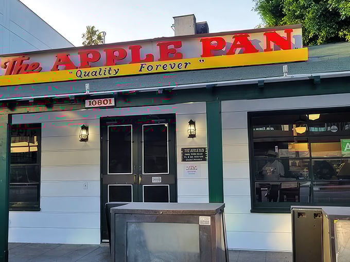 The unassuming white exterior of The Apple Pan stands like a time capsule on Pico Boulevard, its iconic sign promising "Quality Forever" beneath LA's blue skies.