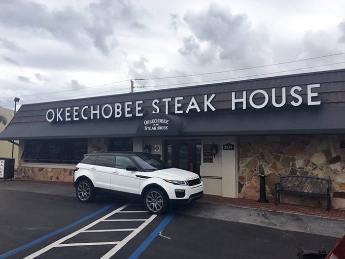 The blue awning of Okeechobee Steakhouse glows like a beacon at dusk, promising carnivorous delights within this Palm Beach institution since 1947.