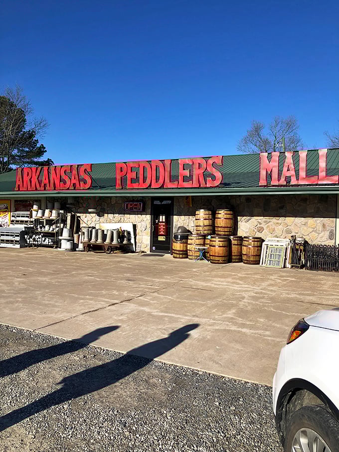 The bright red letters of Arkansas Peddlers stand like a welcoming carnival barker against the sky, with that charming green dinosaur keeping watch over vintage treasures.