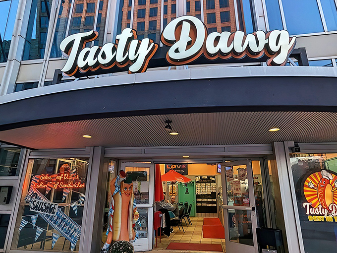 The glowing beacon of Tasty Dawg welcomes hungry patrons with its vibrant signage and life-sized hot dog mascot standing guard, promising delicious adventures within. 