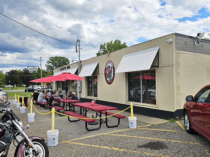 The unassuming tan exterior of Cockeye BBQ hides culinary treasures within, while red picnic tables invite you to dive into smoky delights alfresco.