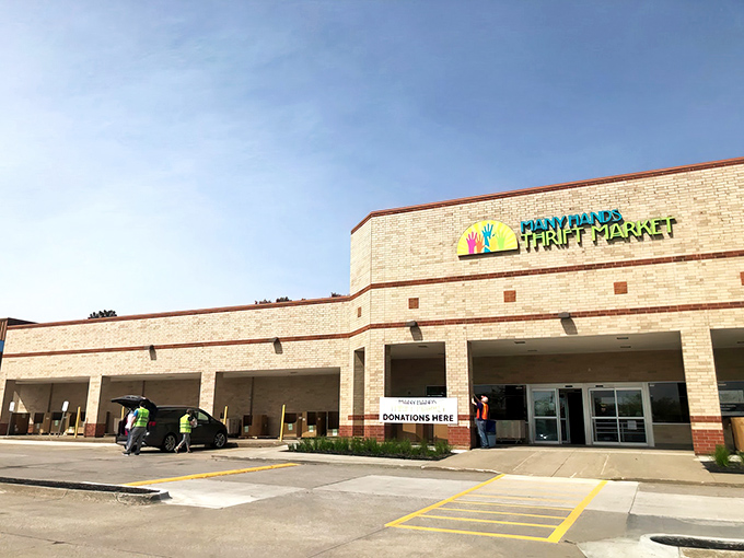 The bright yellow logo featuring colorful hands reaching skyward welcomes bargain hunters like a thrifting bat signal against Clive's clear blue skies.