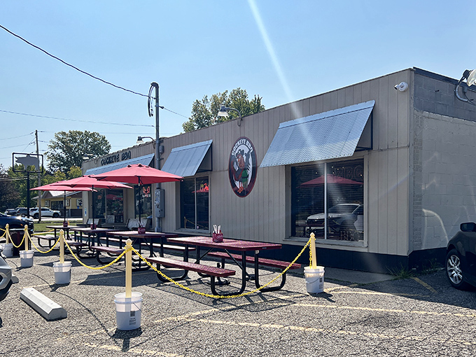 The unassuming tan exterior of Cockeye BBQ hides culinary treasures within, while red picnic tables invite you to dive into smoky delights alfresco.