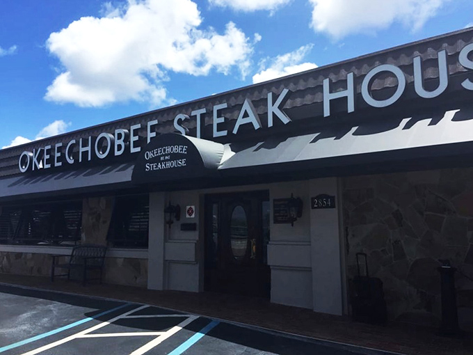 The blue awning of Okeechobee Steakhouse glows like a beacon at dusk, promising carnivorous delights within this Palm Beach institution since 1947.