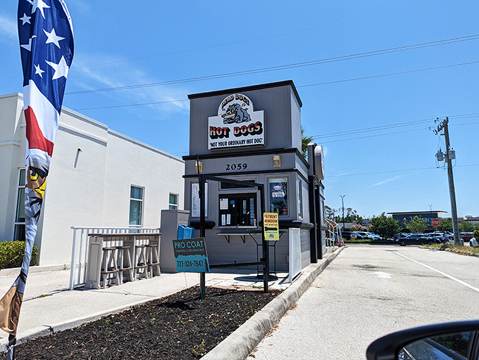 The unassuming gray building with its cartoon bulldog mascot proudly announces: "NOT YOUR ORDINARY HOT DOG." Architectural modesty, culinary boldness.