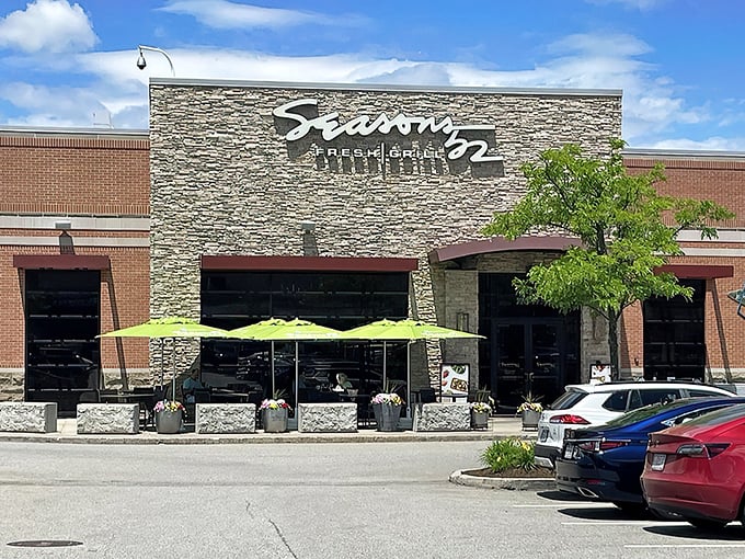 The stone facade of Seasons 52 stands like a culinary lighthouse, beckoning hungry travelers with its warm glow and those unmistakable bright green umbrellas.