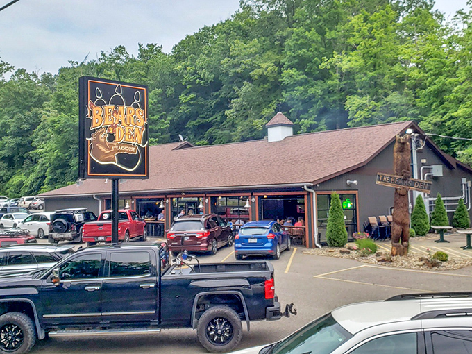 The rustic cabin exterior of Bear's Den Steakhouse promises a wilderness experience with gourmet credentials. That wooden bear statue isn't just decoration&mdash;it's a preview of coming attractions.