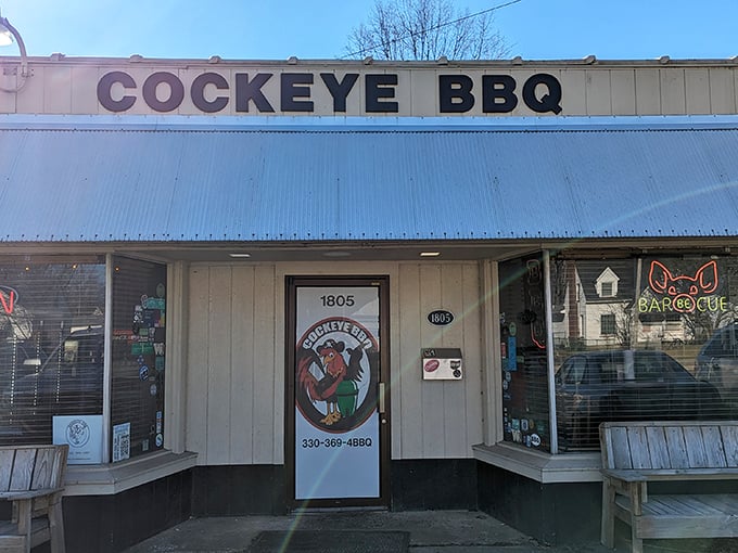 The unassuming tan exterior of Cockeye BBQ hides culinary treasures within, while red picnic tables invite you to dive into smoky delights alfresco.