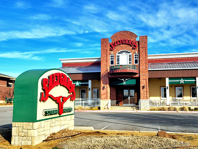 The brick facade of Saltgrass stands like a carnivore's lighthouse, beckoning hungry travelers with its iconic red and green signage against the Oklahoma sky.