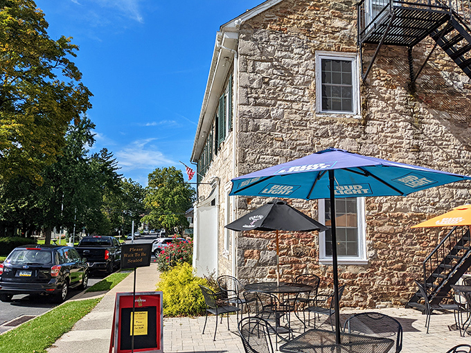 The historic limestone exterior of Duffy's Tavern stands proudly in Boalsburg, with colorful umbrellas inviting you to enjoy Pennsylvania sunshine while dining al fresco.