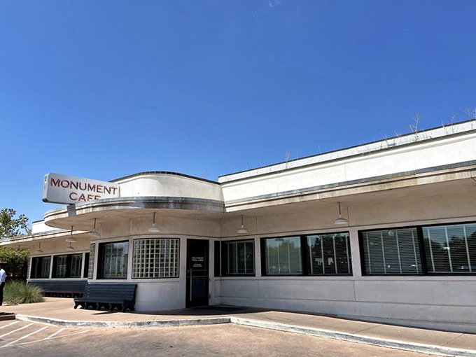 The iconic curved facade of Monument Cafe stands like a mid-century mirage against the Texas sky, promising comfort food paradise within.