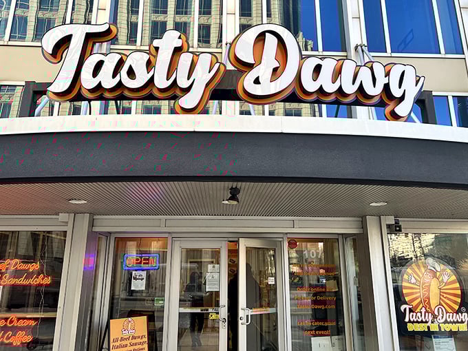 The glowing beacon of Tasty Dawg welcomes hungry patrons with its vibrant signage and life-sized hot dog mascot standing guard, promising delicious adventures within. 
