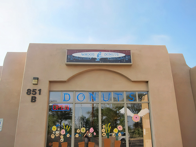 The unassuming adobe exterior of Whoo's Donuts, where Santa Fe's sweetest treasures await behind that neon "OPEN" sign. Donut paradise incognito!