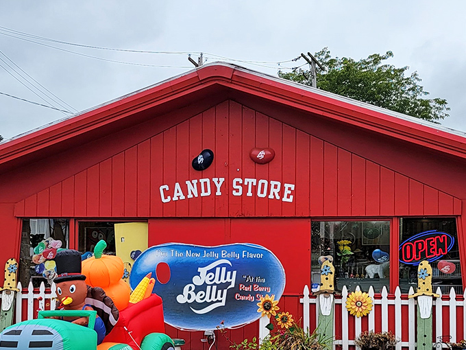 The bright red exterior of Red Berry Candy Shop stands like a beacon of sweetness, complete with white picket fence and cheerful garden decorations.