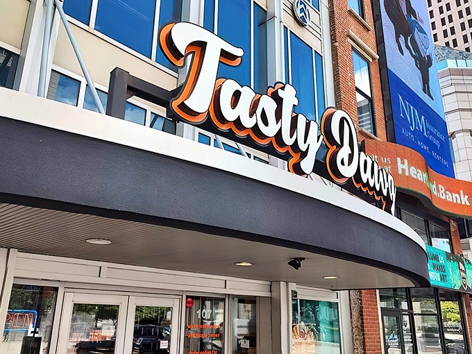 The glowing beacon of Tasty Dawg welcomes hungry patrons with its vibrant signage and life-sized hot dog mascot standing guard, promising delicious adventures within. 
