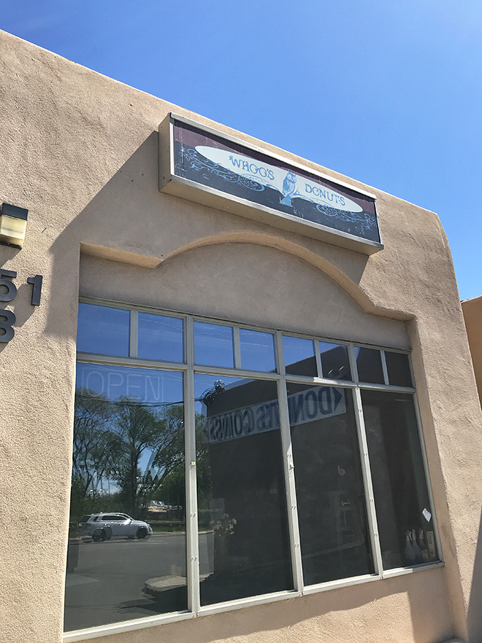 The unassuming adobe exterior of Whoo's Donuts, where Santa Fe's sweetest treasures await behind that neon "OPEN" sign. Donut paradise incognito!