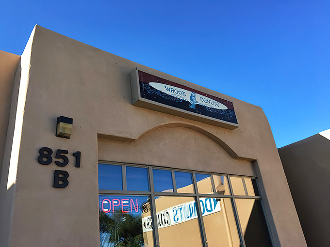 The unassuming adobe exterior of Whoo's Donuts, where Santa Fe's sweetest treasures await behind that neon "OPEN" sign. Donut paradise incognito!
