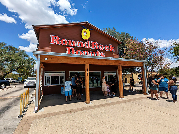 The iconic wooden and limestone facade of Round Rock Donuts stands proudly under Texas skies, beckoning donut pilgrims with its famous red signage.