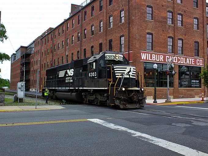 A Norfolk Southern locomotive rumbles past the iconic Wilbur Chocolate building, where sweet history meets small-town charm in a perfect Pennsylvania moment.