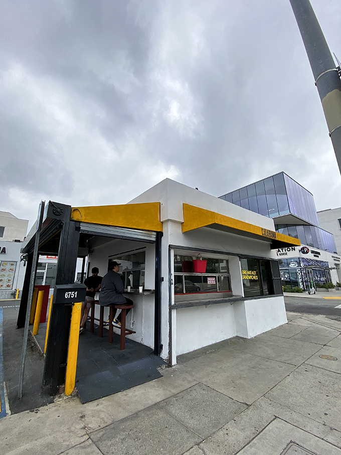 The corner of Santa Monica Boulevard where breakfast dreams come true. That yellow awning is like a culinary lighthouse guiding hungry souls to sandwich salvation.
