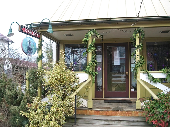 The charming yellow exterior of The Rail Stop beckons like an old friend, promising comfort and culinary delights beside that distinctive red sign.