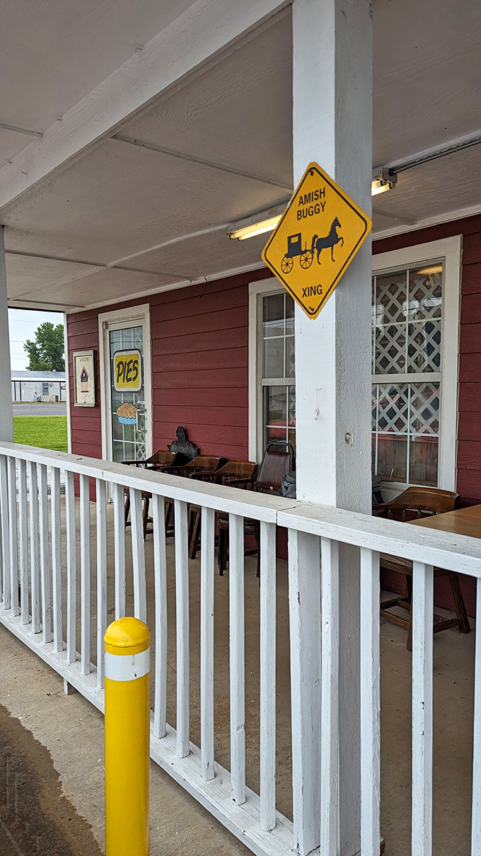 The welcoming front porch of Amish Country Store beckons with its classic red siding, white railings, and that charming "Amish Buggy Xing" sign that promises authentic flavors await inside.