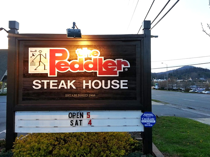 The iconic Peddler sign welcomes hungry travelers with its warm glow and glass-enclosed fire feature&mdash;a beacon of promised culinary delights in Boone's mountain landscape.