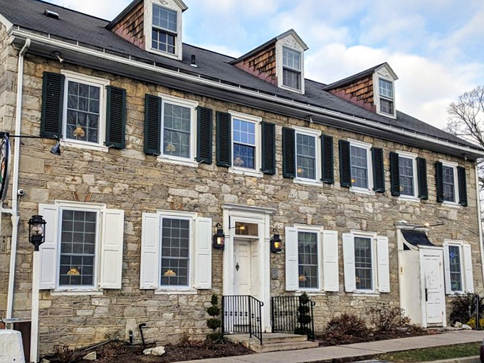The historic limestone exterior of Duffy's Tavern stands proudly in Boalsburg, with colorful umbrellas inviting you to enjoy Pennsylvania sunshine while dining al fresco.