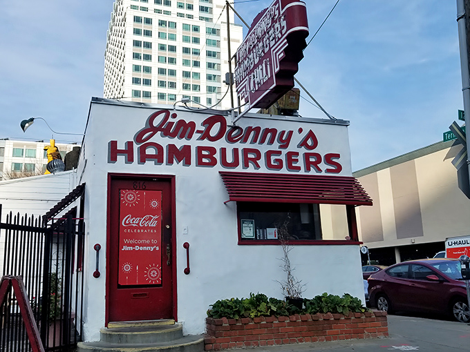 That iconic red sign against the blue California sky is like a beacon for burger lovers. Jim-Denny's modest exterior hides culinary greatness within.