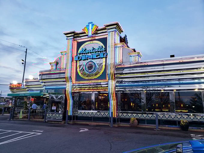 The neon-drenched facade of Marietta Diner glows like a beacon for hungry souls, a chrome-clad time machine promising comfort food and nostalgia.