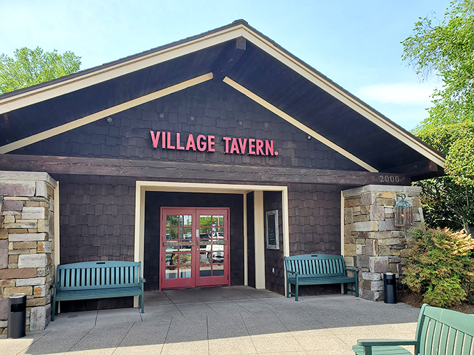 The rustic stone fa&ccedil;ade and welcoming teal benches at Village Tavern's entrance promise comfort before you even cross the threshold.